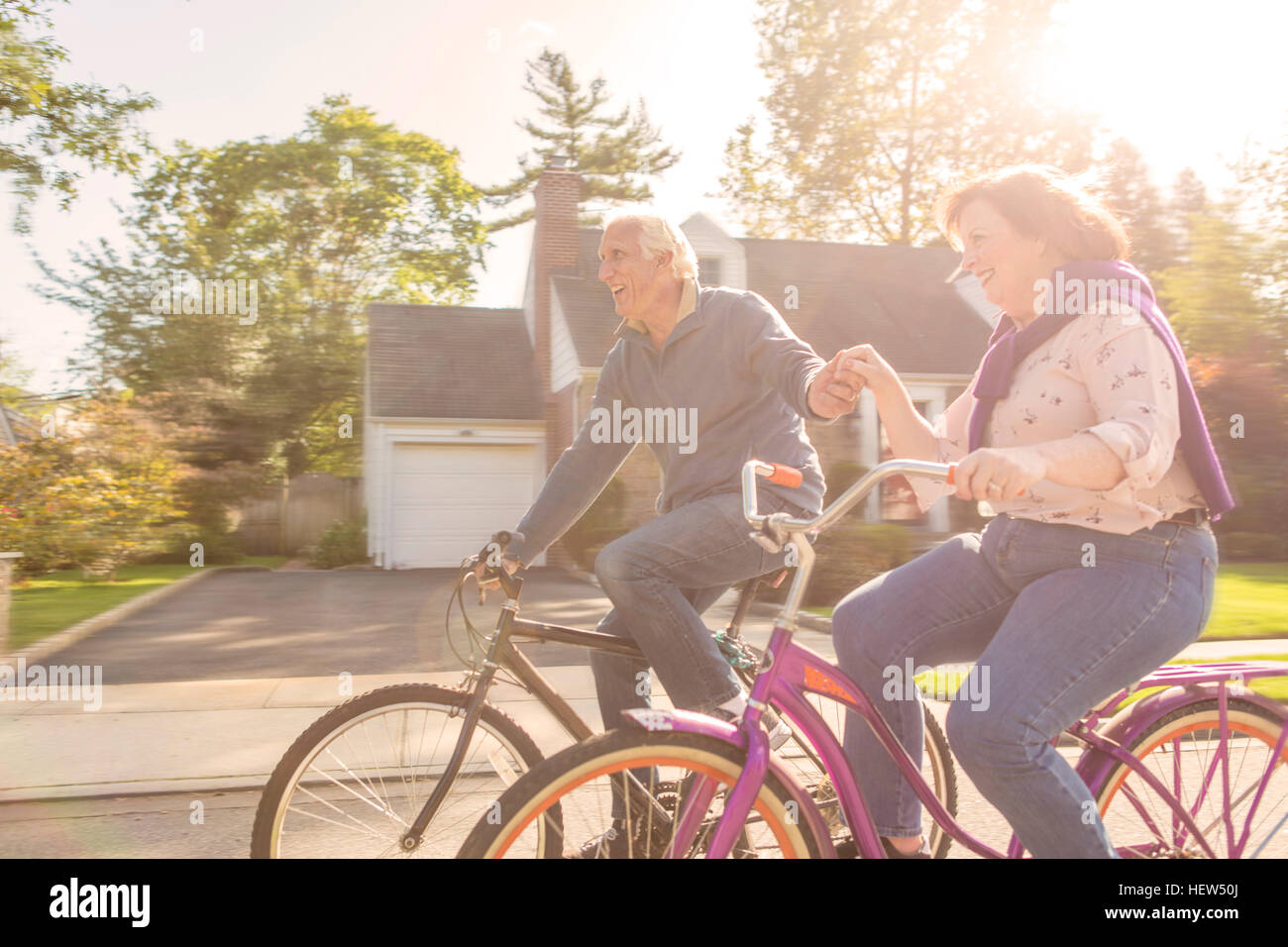 Romantic senior couple holding hands cycling along suburban road Stock ...