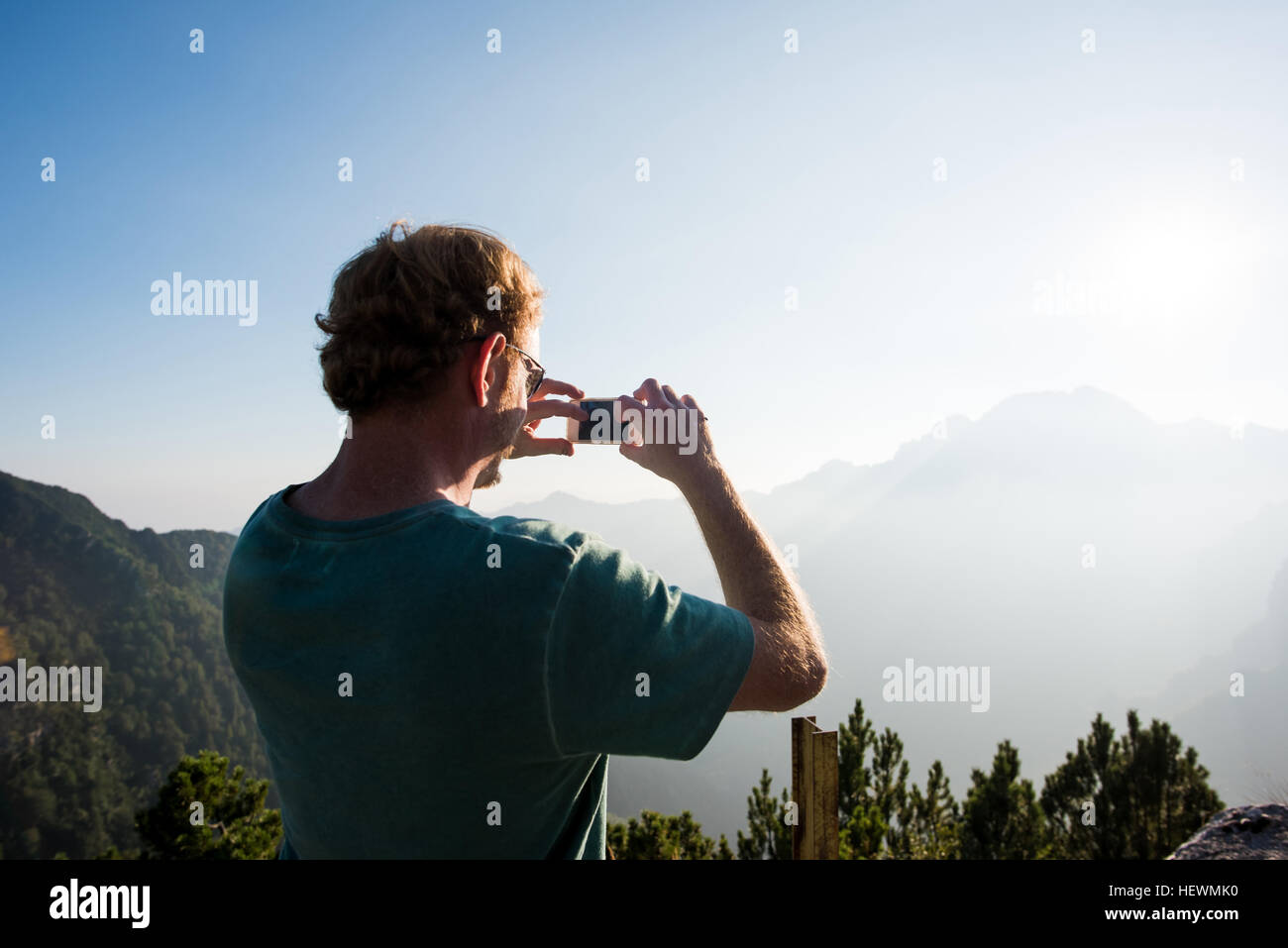 Rear view of man taking photograph of mountains, Passo Maniva, Italy ...