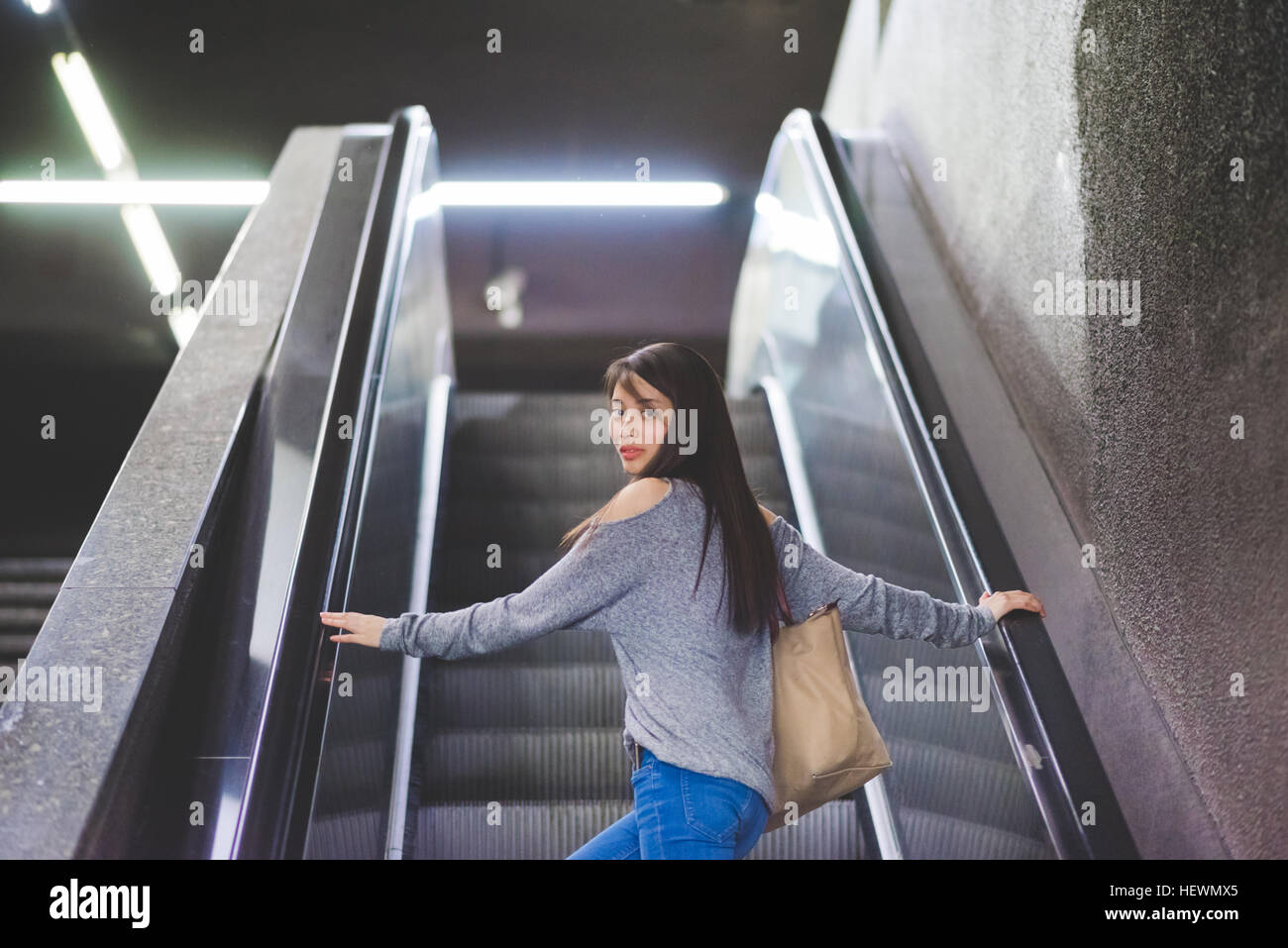 Portrait of young woman looking back from city escalator Stock Photo ...