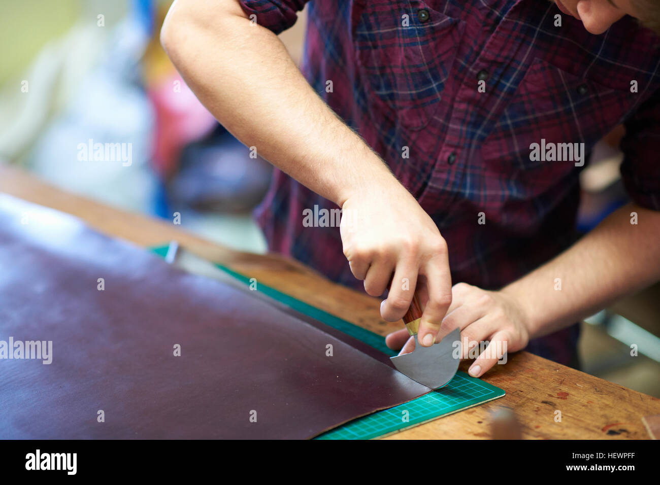 Male worker in leather workshop, using cutting tool to cut leather, mid ...