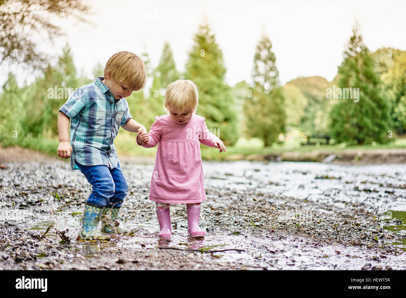 Brother and sister holding hands splashing in muddy puddle Stock Photo ...