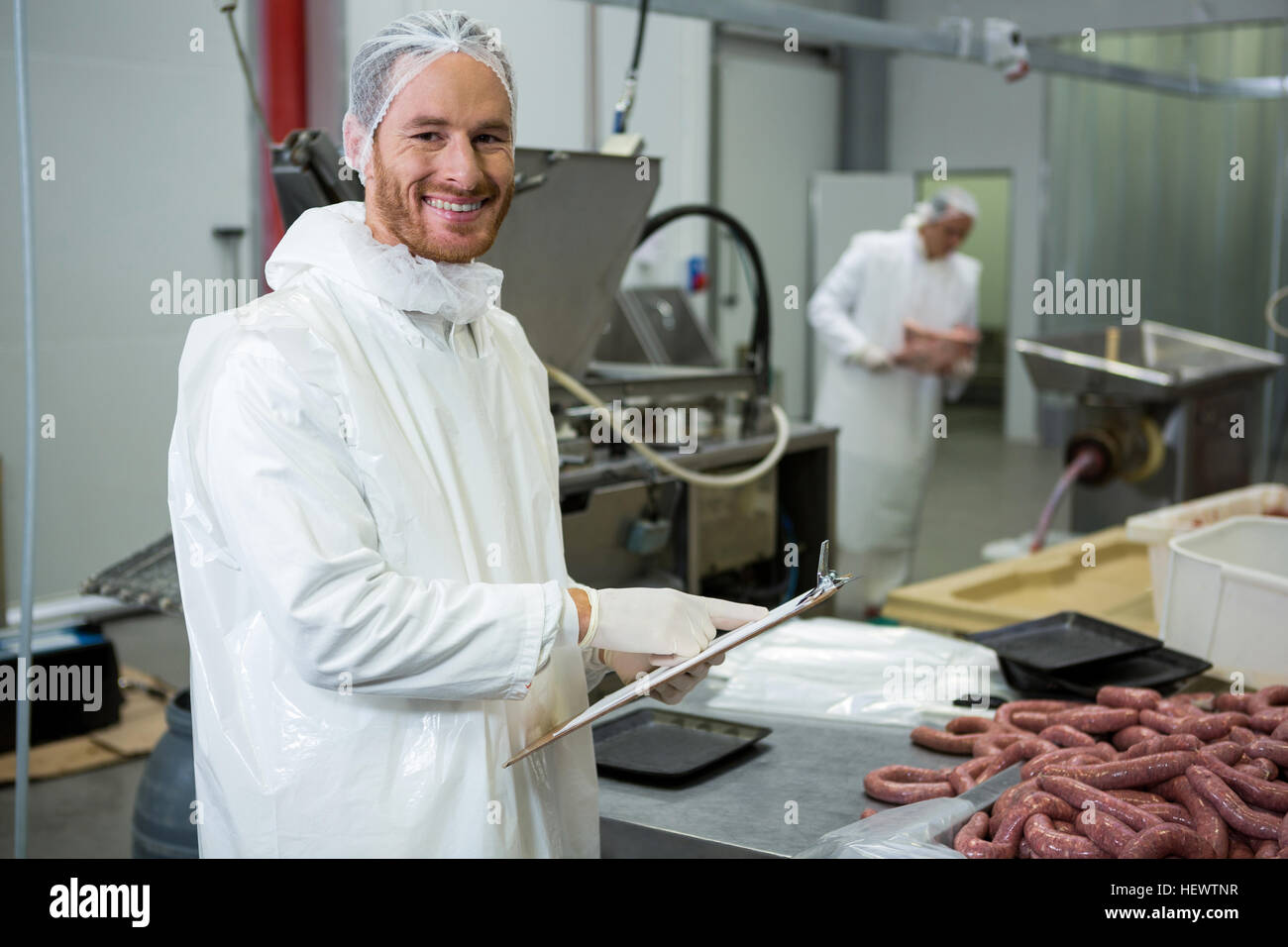 Portrait of male butcher maintaining records on clipboard at meat ...