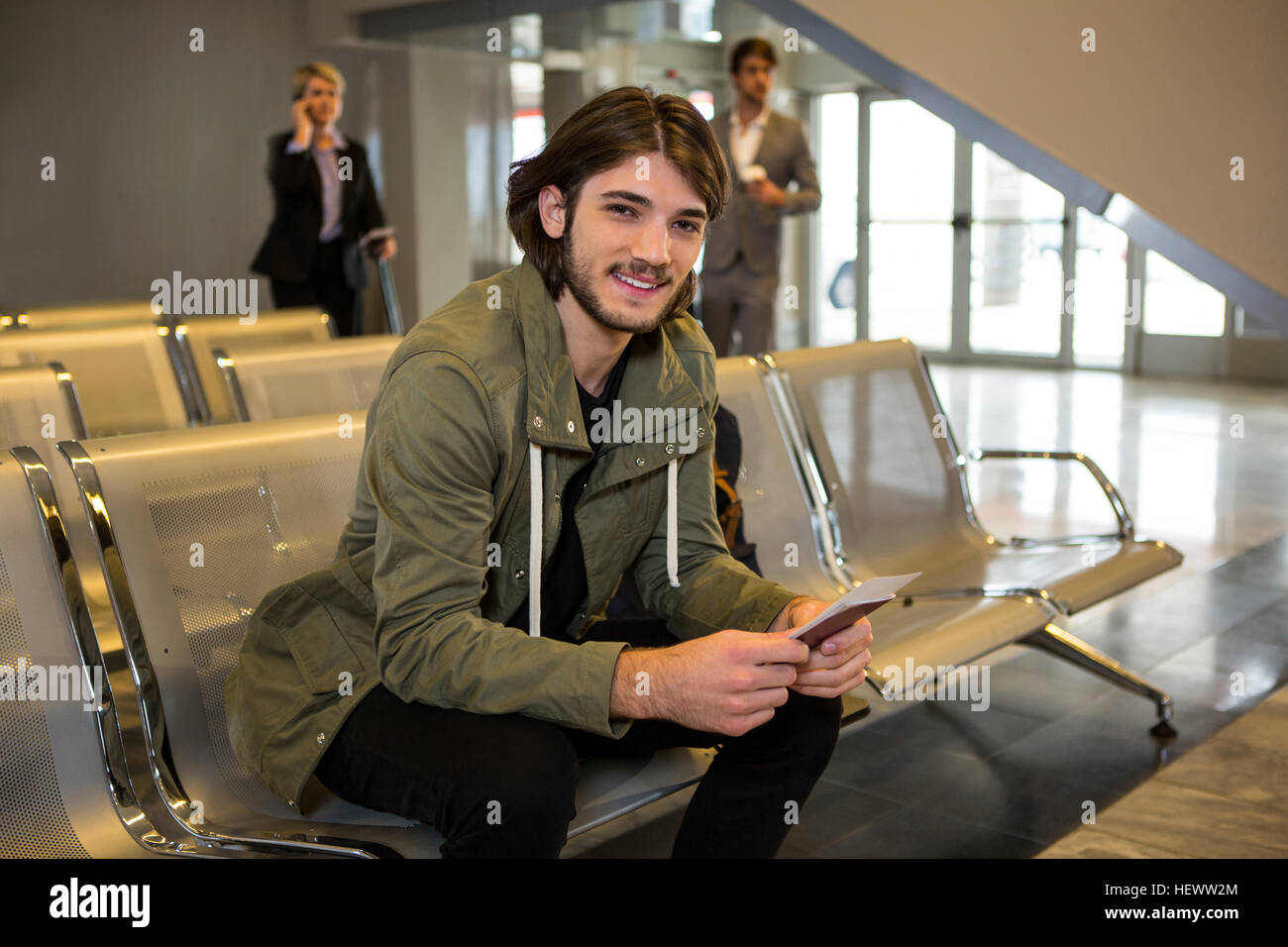 Man with passport and boarding pass sitting in waiting area at airport ...