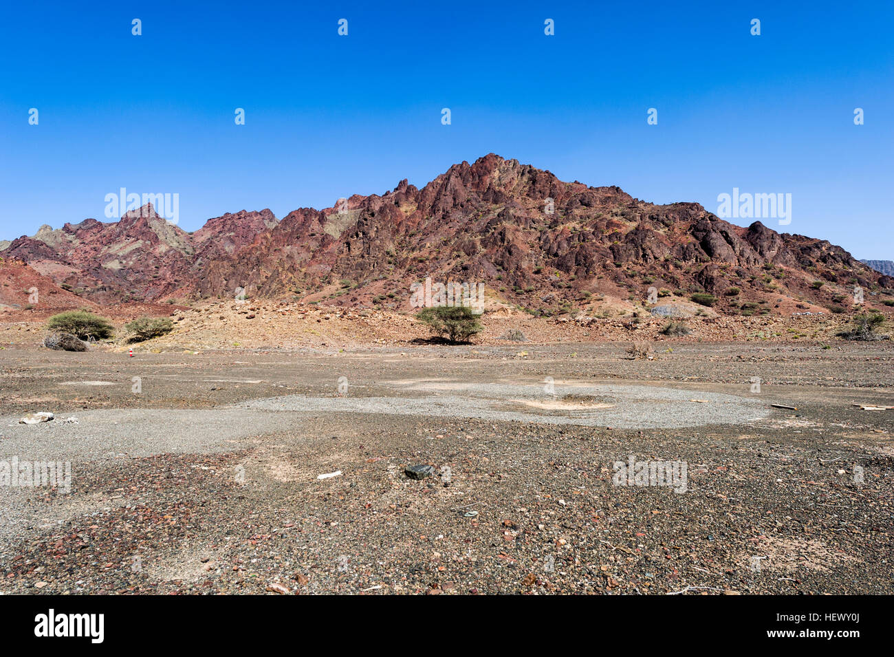 A red volcanic mountain rises from a gravel plain in the desert Stock ...