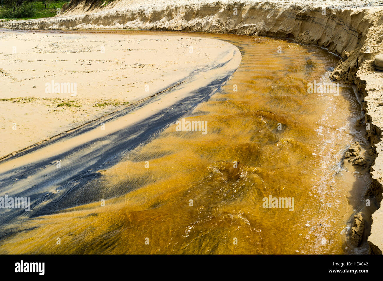 A freshwater stream flowing over the sand on a beach into the ocean ...