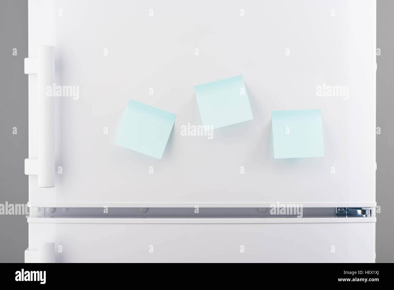 Three blank light blue sticky paper notes on white refrigerator door ...