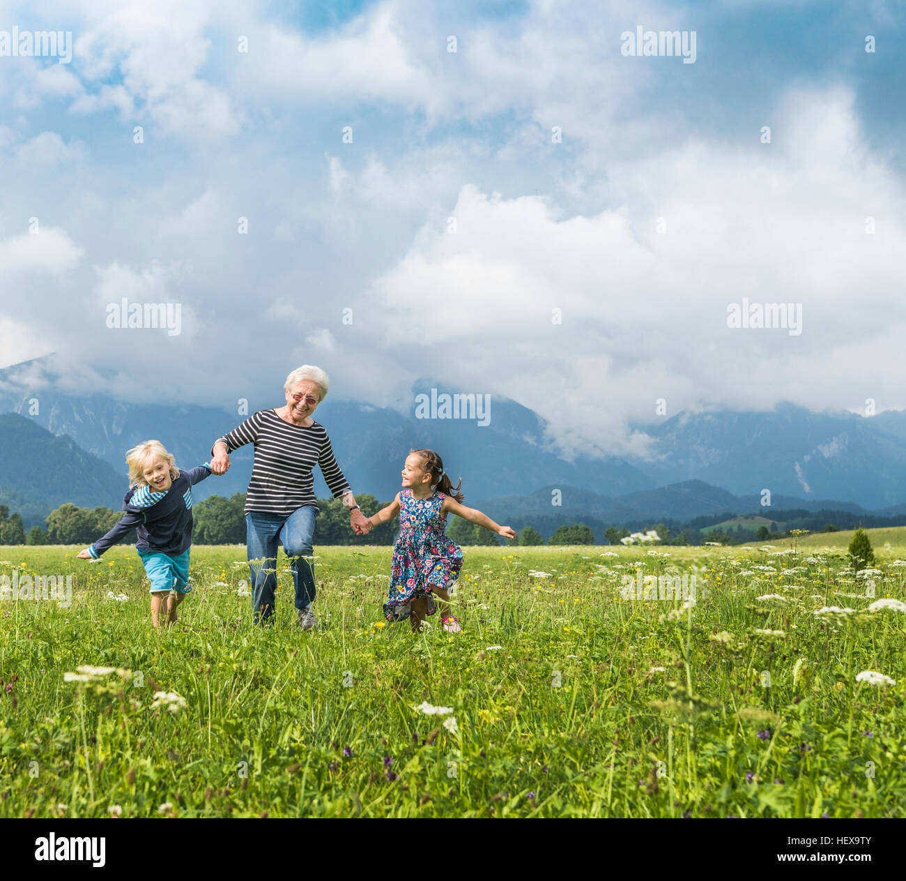 Grandmother and grandchildren running in field holding hands, Fuessen ...