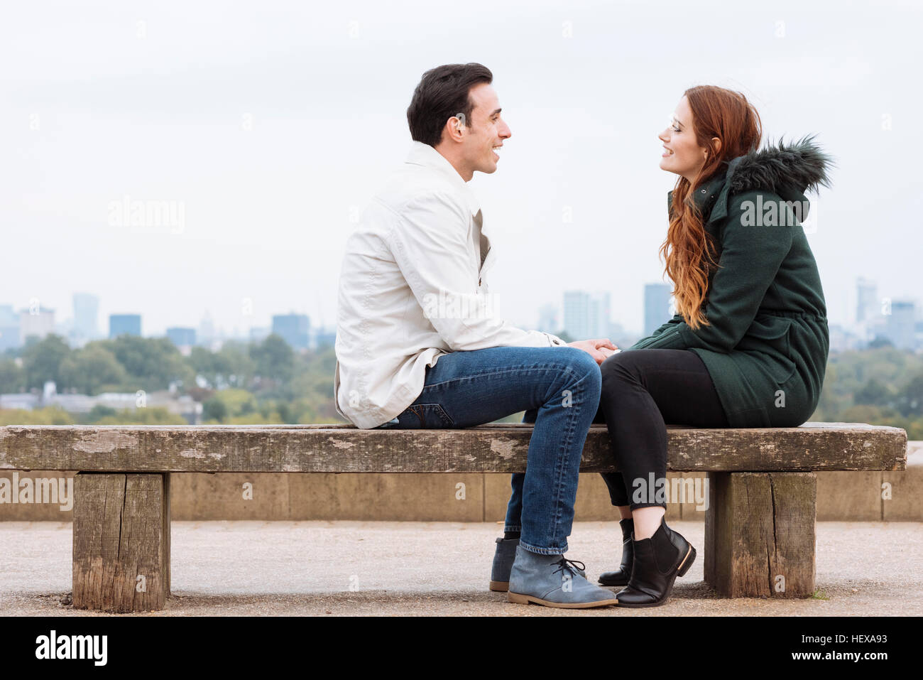 Side view of couple sitting face to face on bench Stock Photo - Alamy