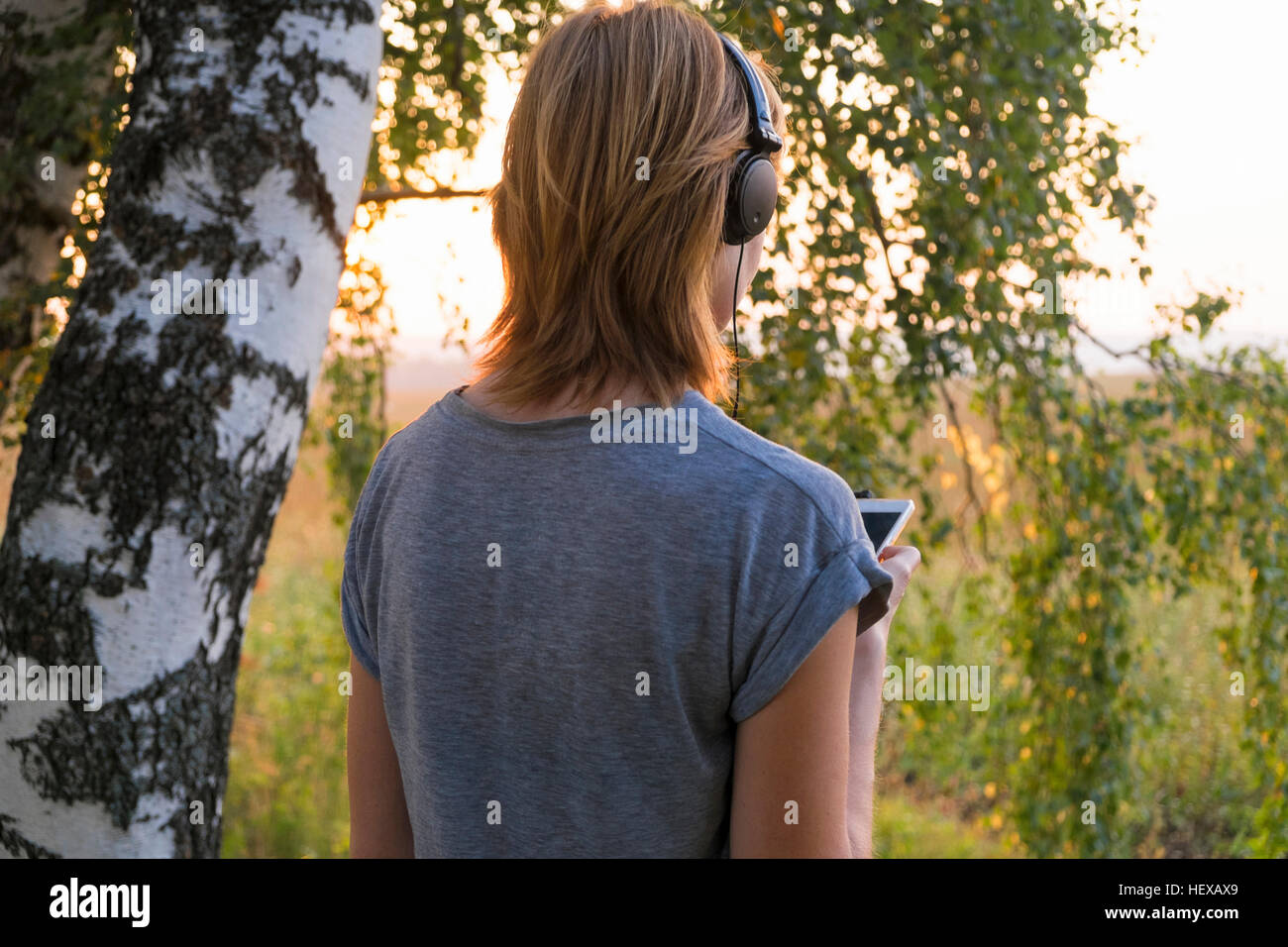 Rear view of woman listening to headphones looking out from woodland ...
