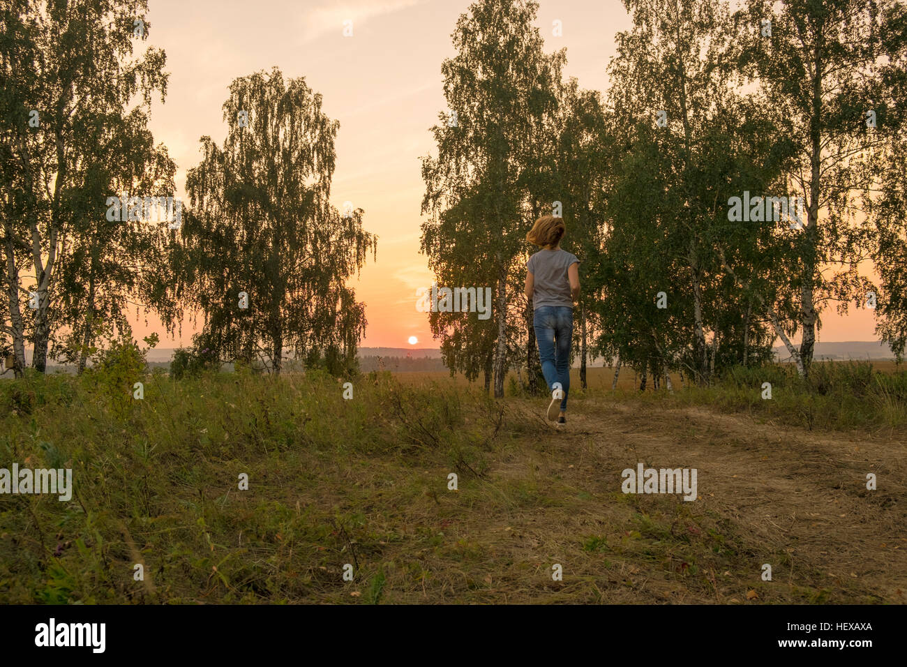Rear view of woman running along rural dirt track at sunset Stock Photo ...