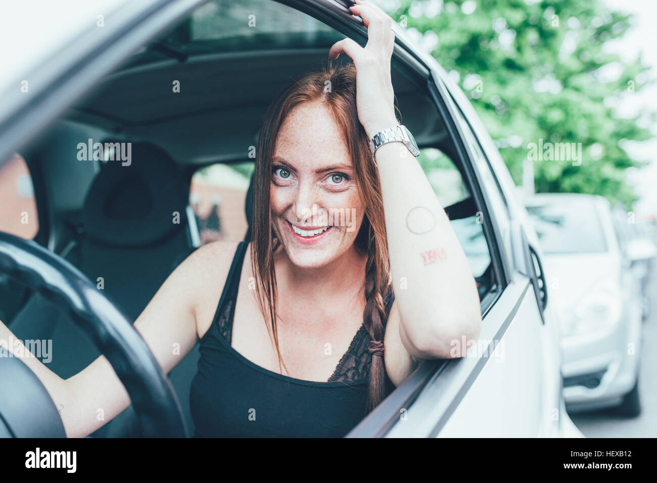 Portrait of young woman with long red hair and freckles at car window ...