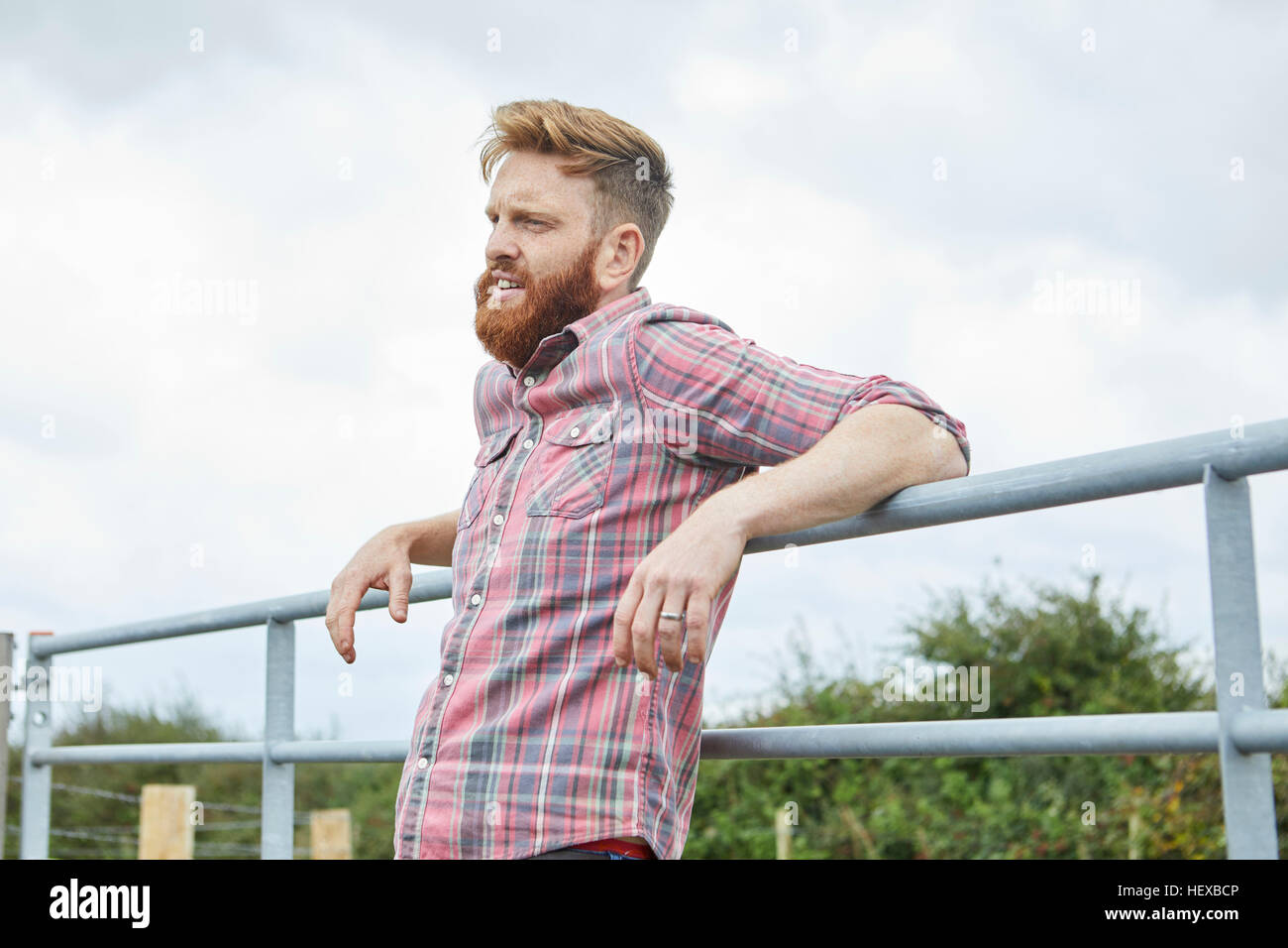 Man leaning against farm gate looking away Stock Photo - Alamy