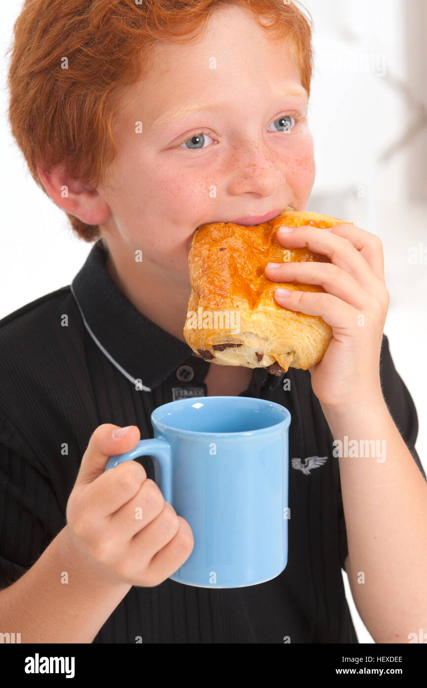 MODEL RELEASED. Boy eating pain au chocolate and holding mug Stock ...