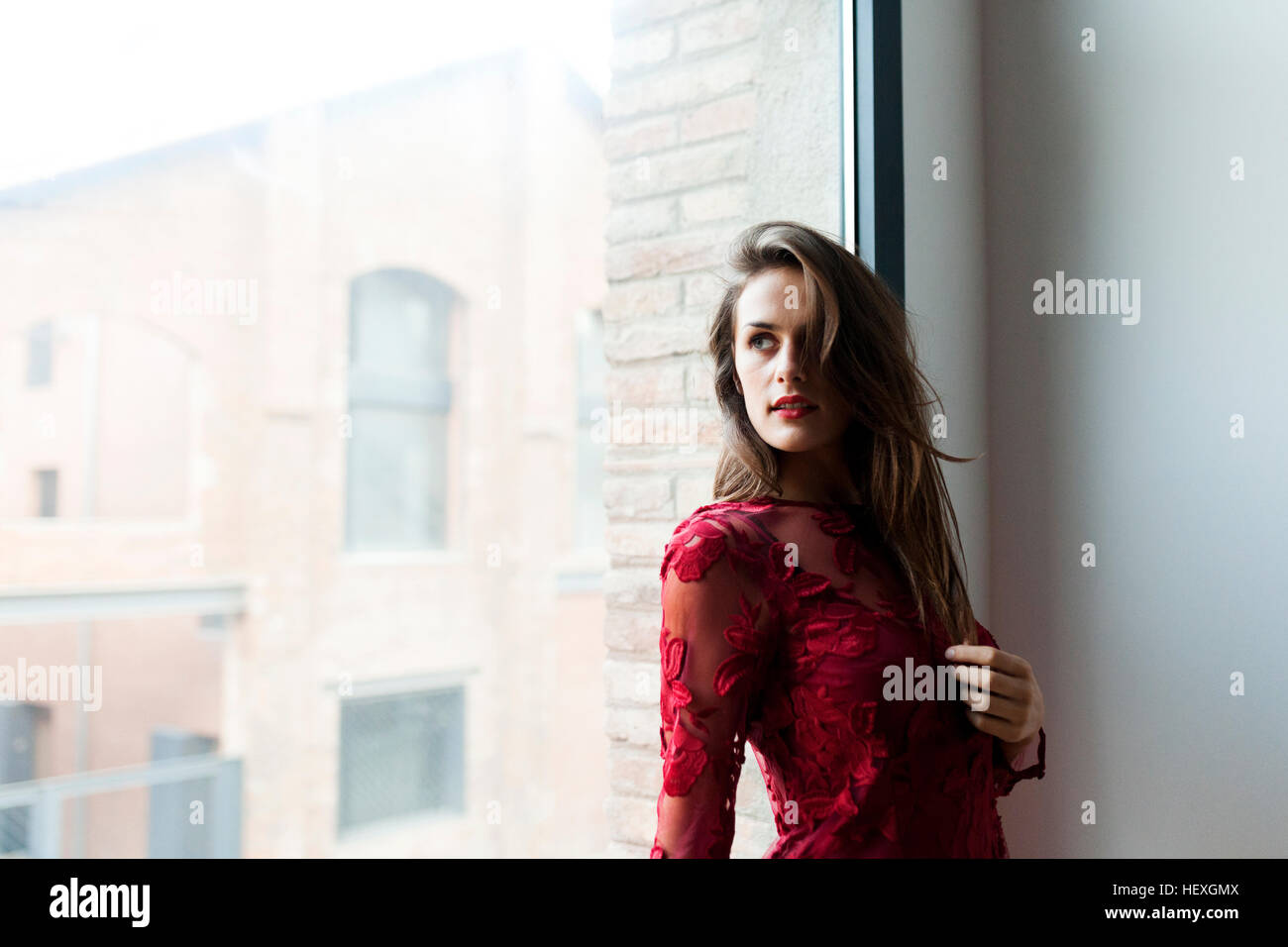 Beautiful young woman wearing red dress at a window Stock Photo - Alamy