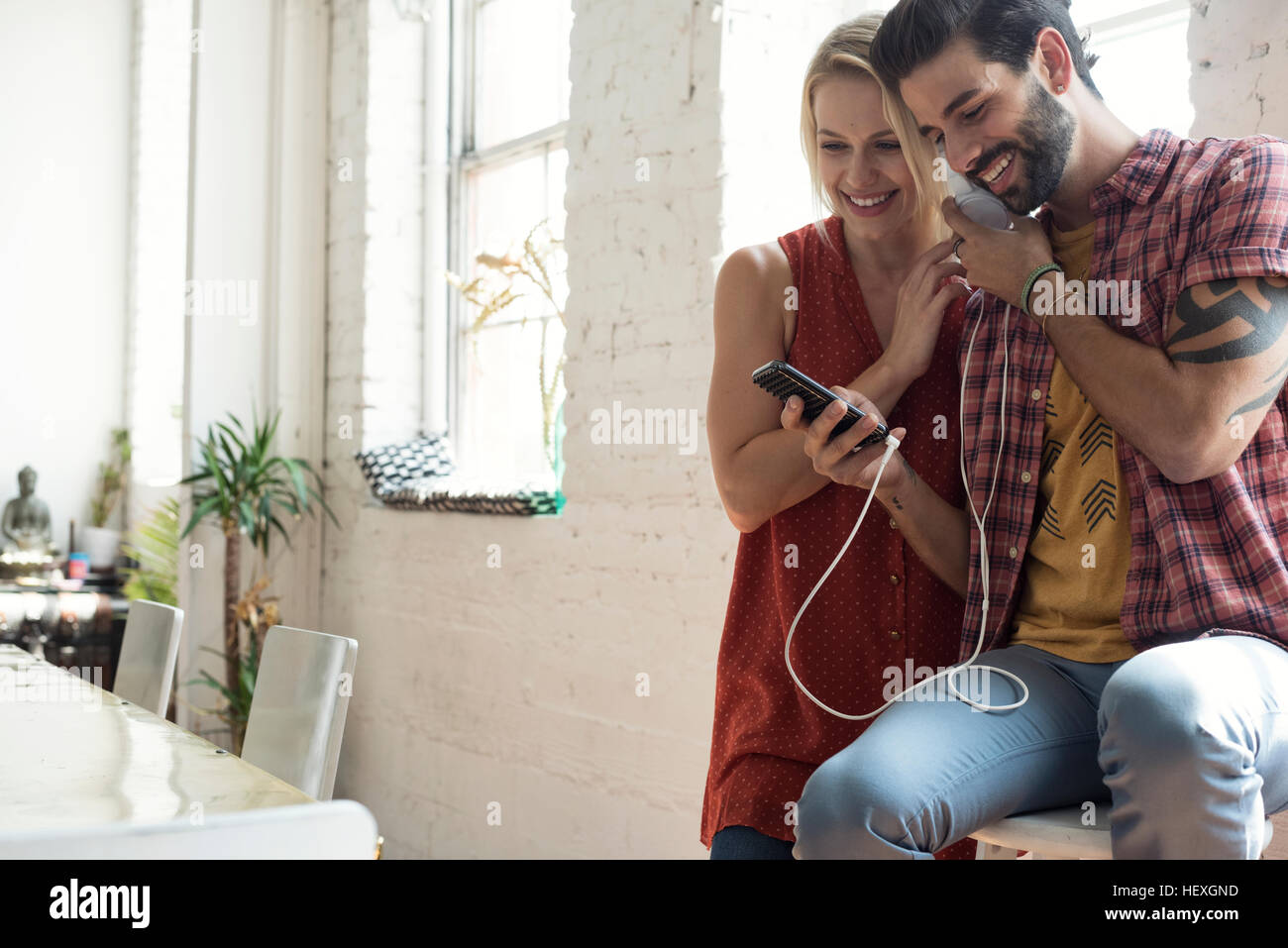 Happy young couple with cell phone at the window sharing headphones ...