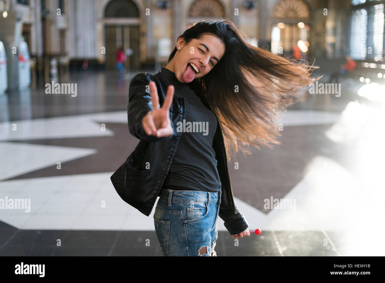 Portrait of exuberant young woman with lollipop in station concourse ...