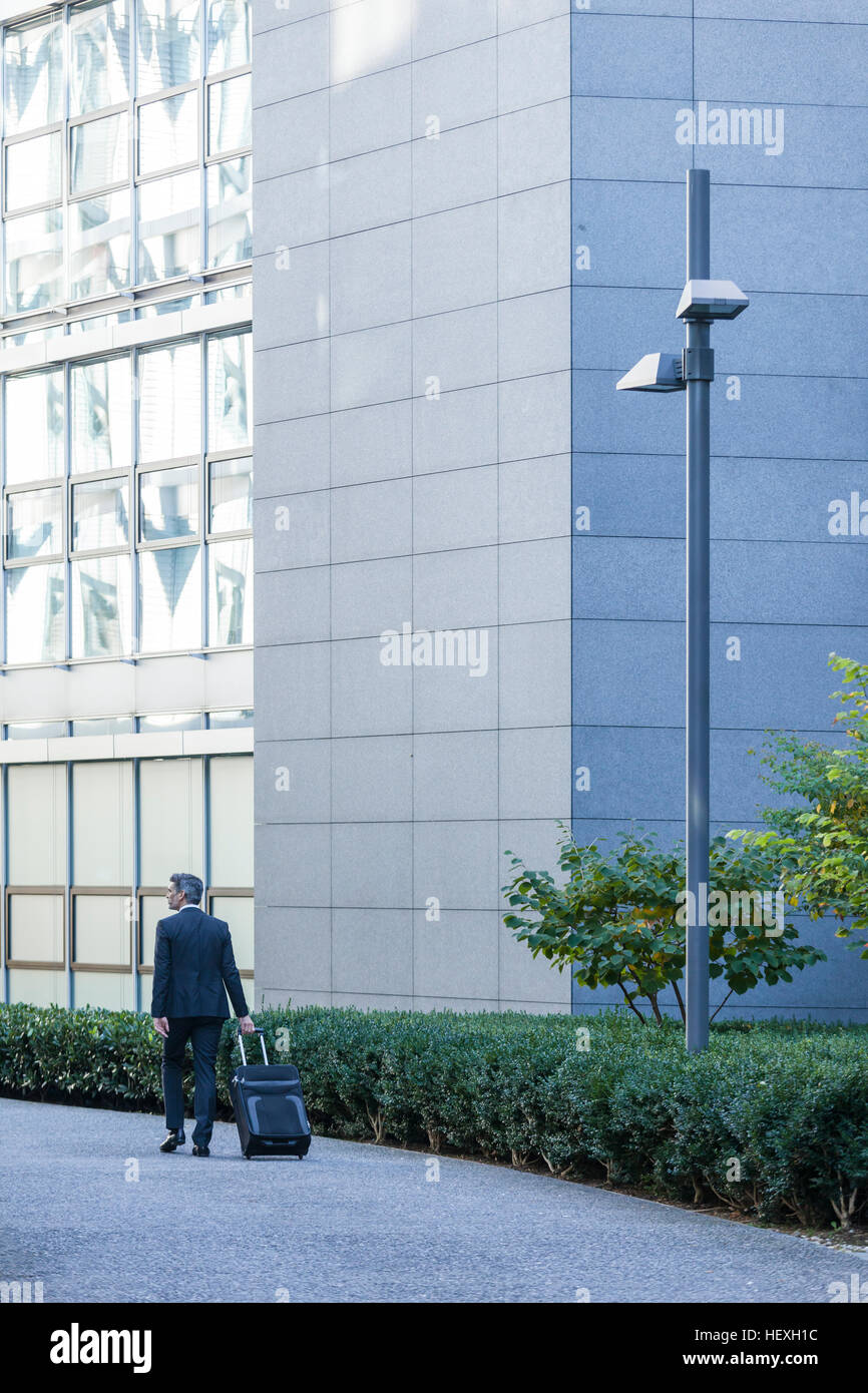 Businessman walking with suitcase outdoors Stock Photo - Alamy