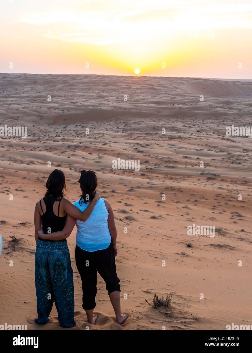Oman, Al Raka, two young women standing arm in arm on a desert dune ...