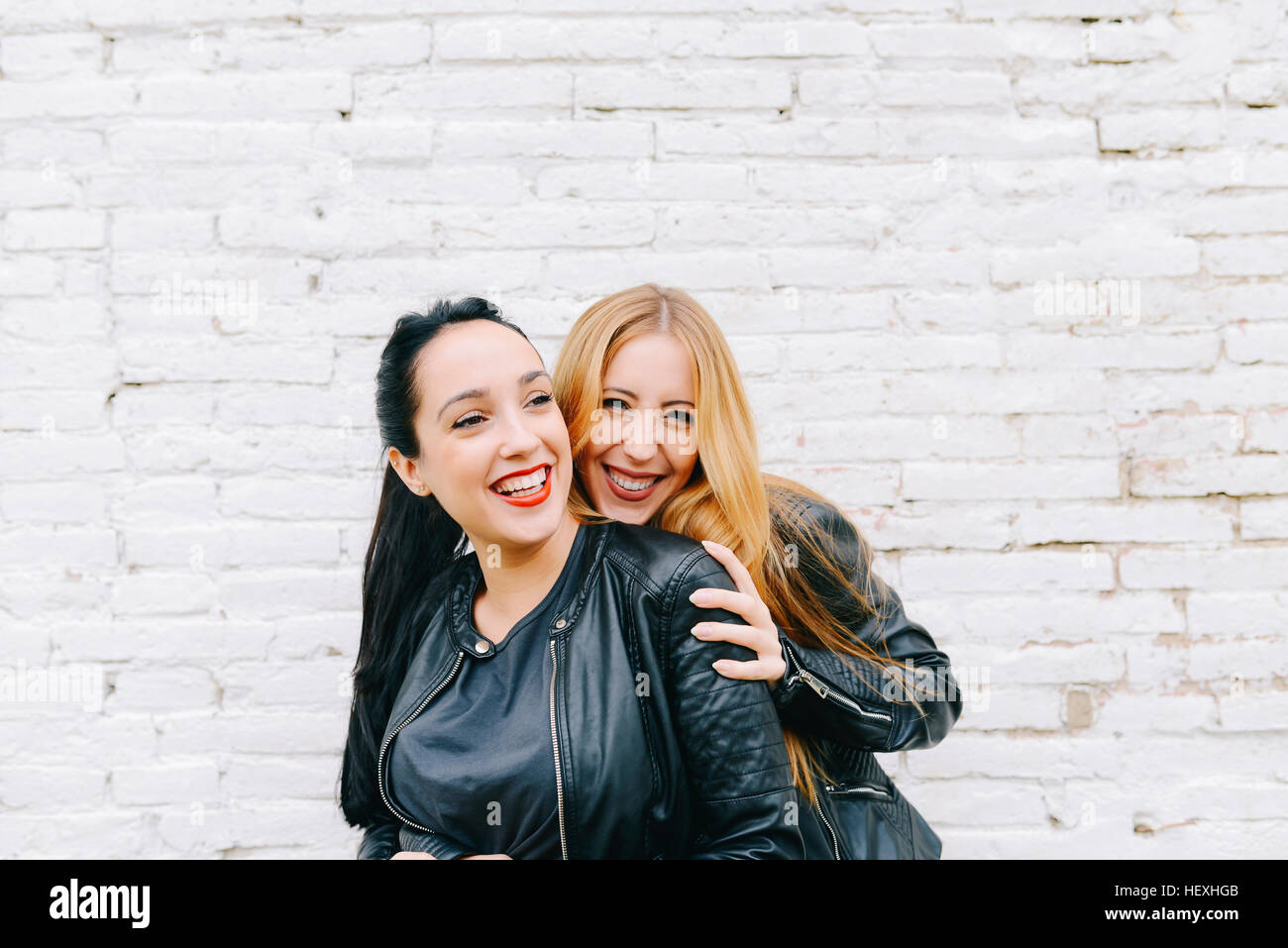 Two laughing young women in front of white brick wall Stock Photo - Alamy