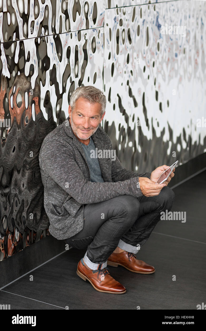 Confident businessman crouching at rippled wall with tablet Stock Photo ...
