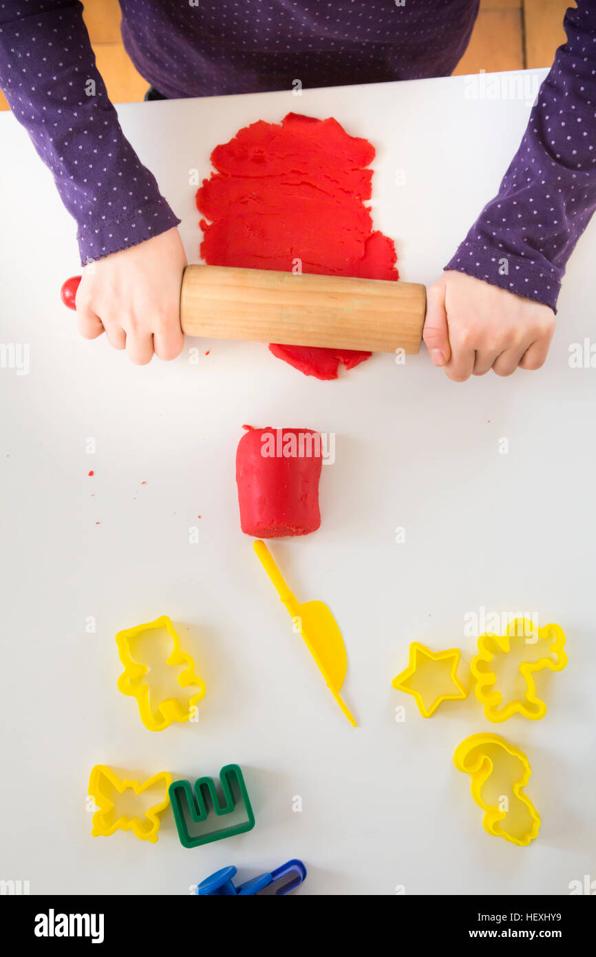 Little girl rolling out red modeling clay, top view Stock Photo - Alamy