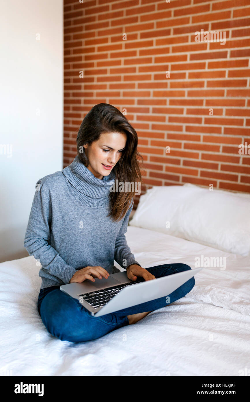 Young woman sitting on bed using laptop Stock Photo - Alamy