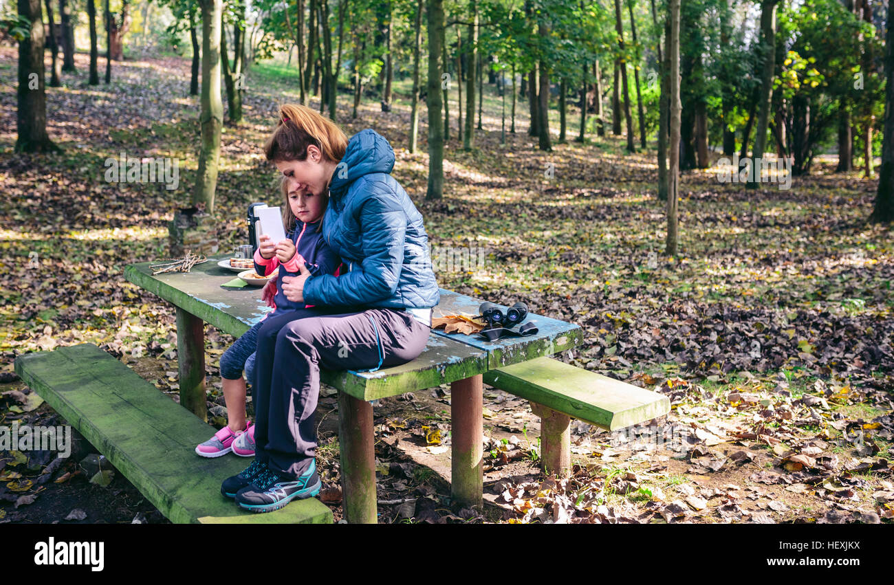 Mother and little daughter sitting at picnic place in the forest playing with smartphone Stock ...