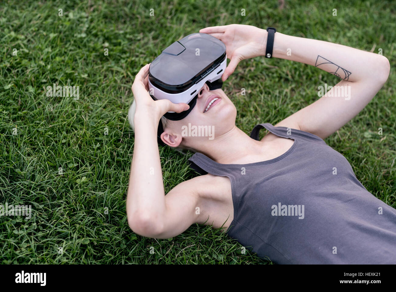 Young woman lying on a meadow wearing Virtual Reality Glasses outdoors ...