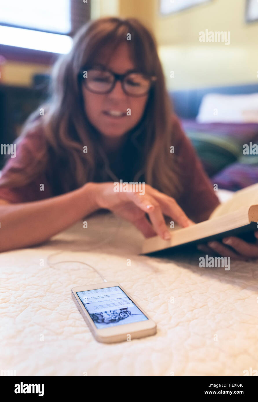 Woman with cell phone reading a book at home Stock Photo - Alamy