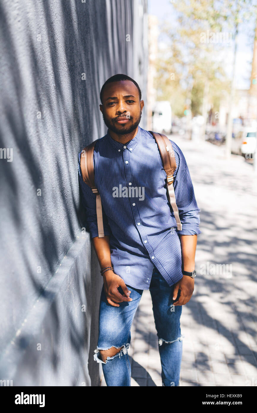 Man with backpack leaning against facade Stock Photo - Alamy