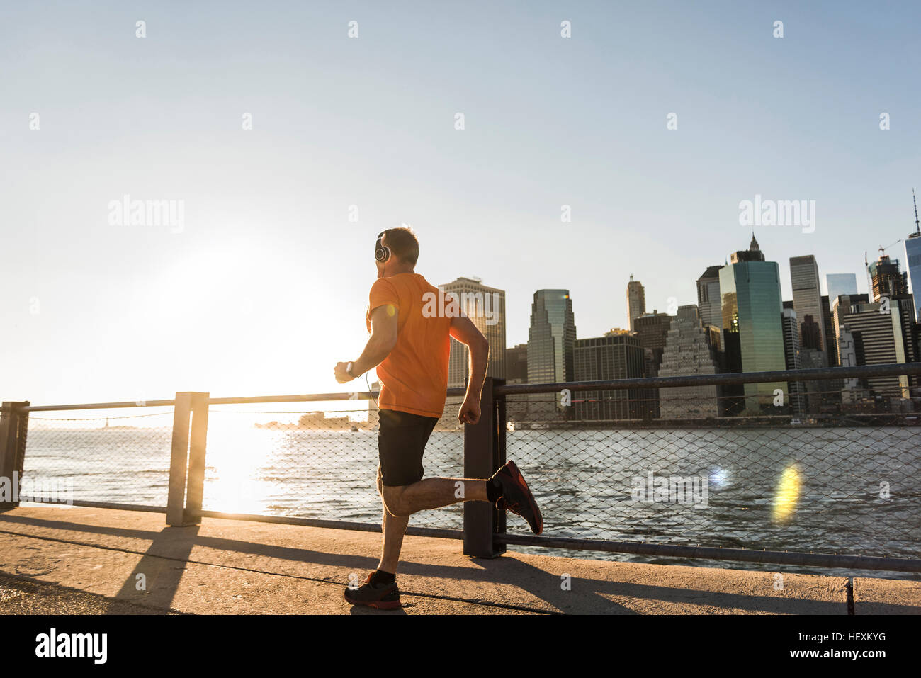 USA, Brooklyn, man jogging in front of Manhattan skyline in the evening ...