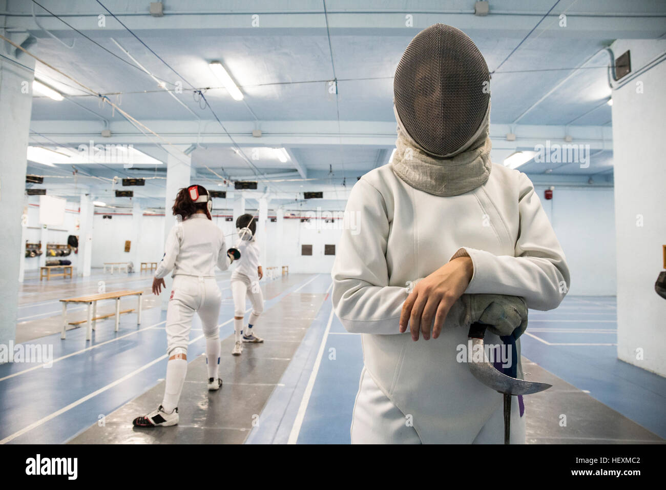Female fencer wearing fencing mask with fencing match in the background ...