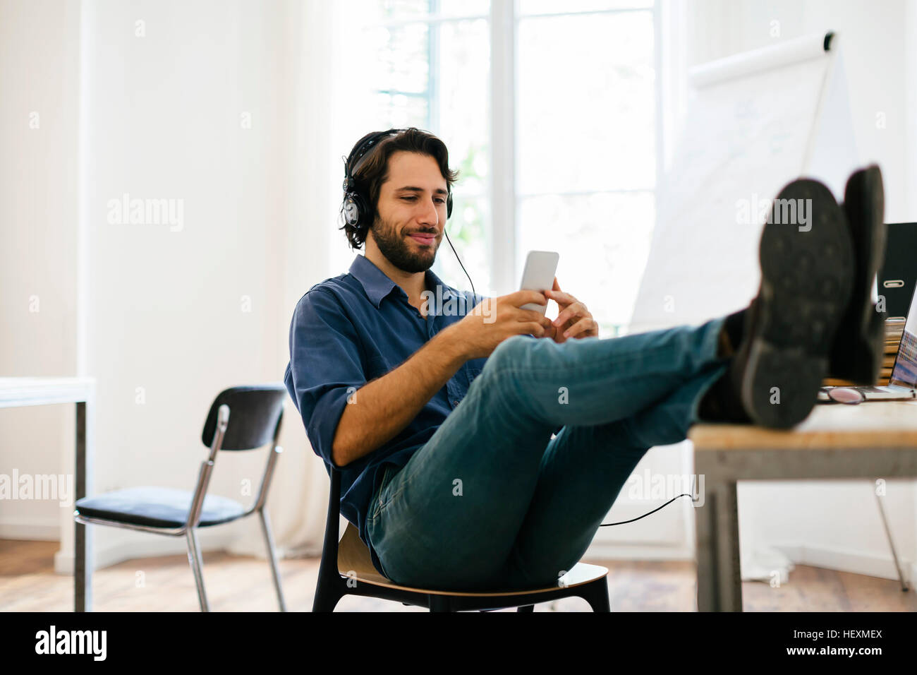Businessman in office using headphones and smart phone, feet up Stock ...