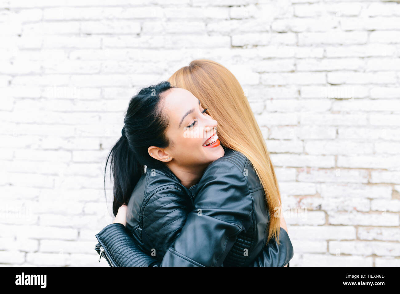 Two young women hugging in front of white brick wall Stock Photo - Alamy