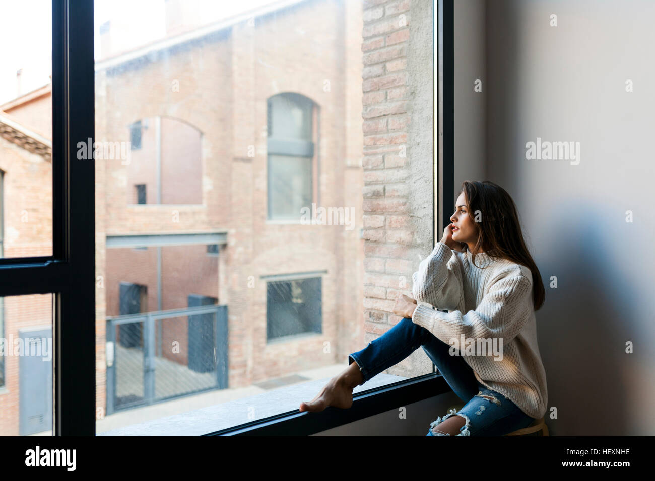 Young woman sitting at a window looking out Stock Photo - Alamy