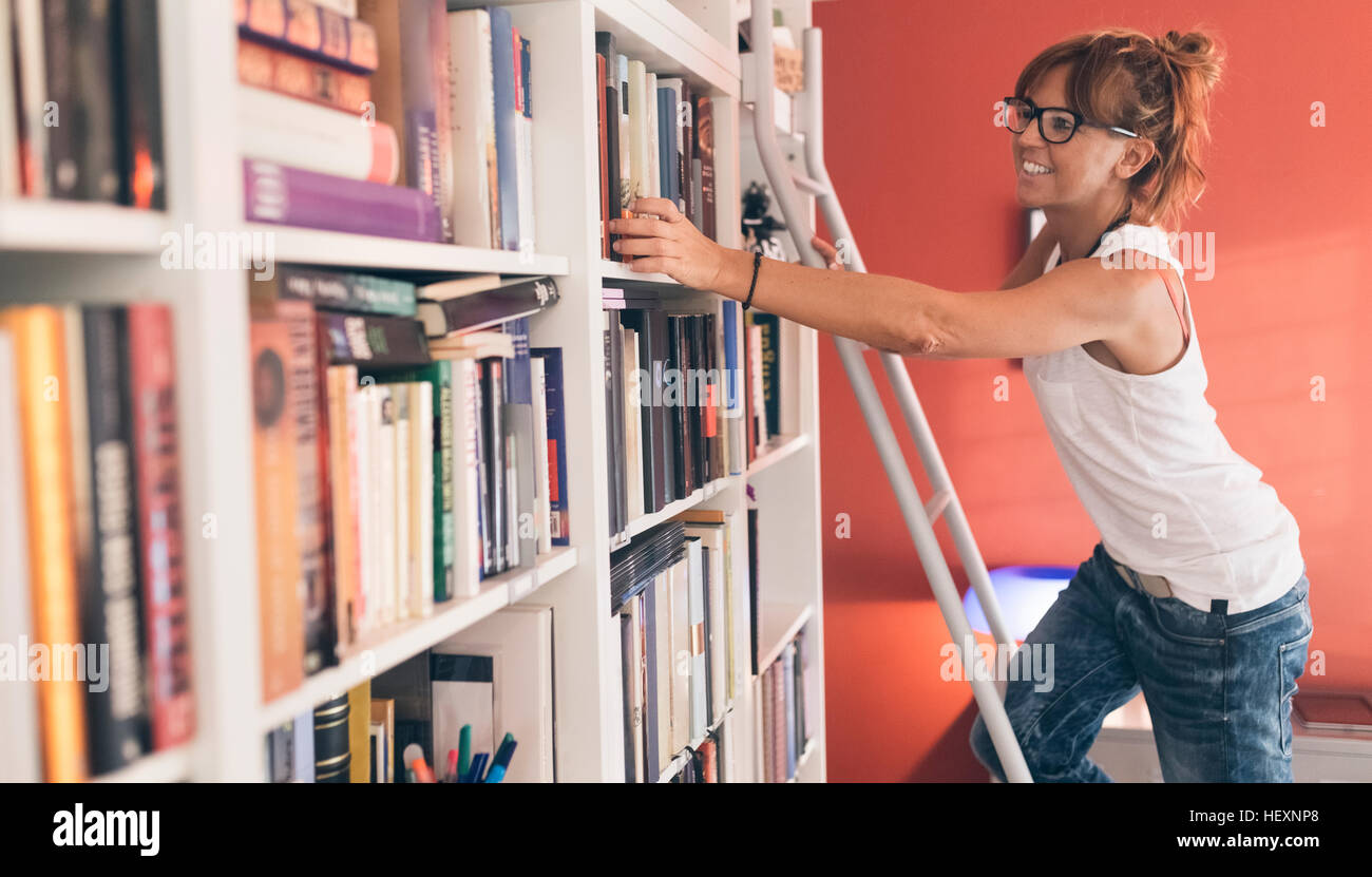 Woman taking a book from bookshelf Stock Photo - Alamy