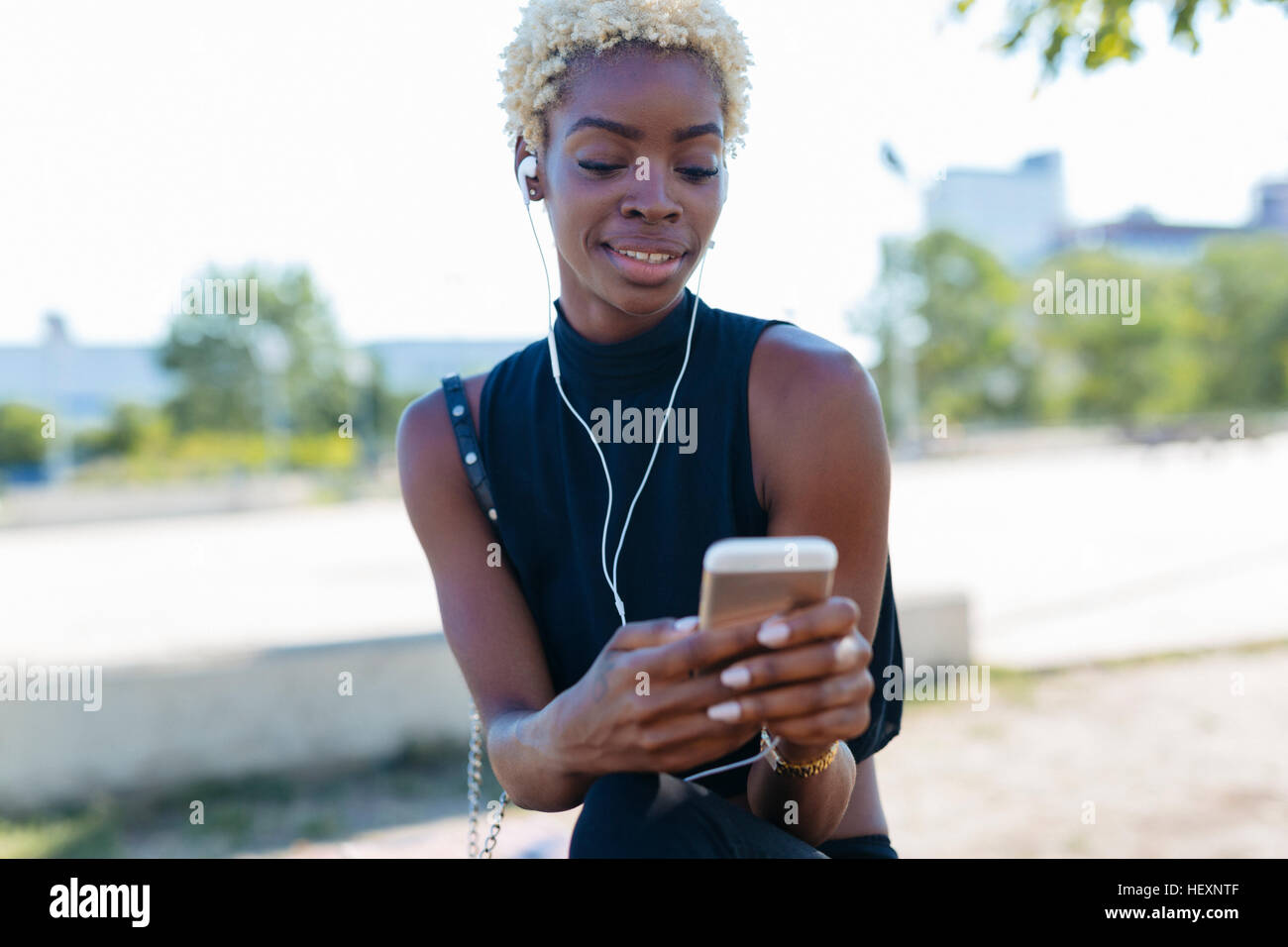 Smiling young woman with cell phone and earbuds Stock Photo - Alamy