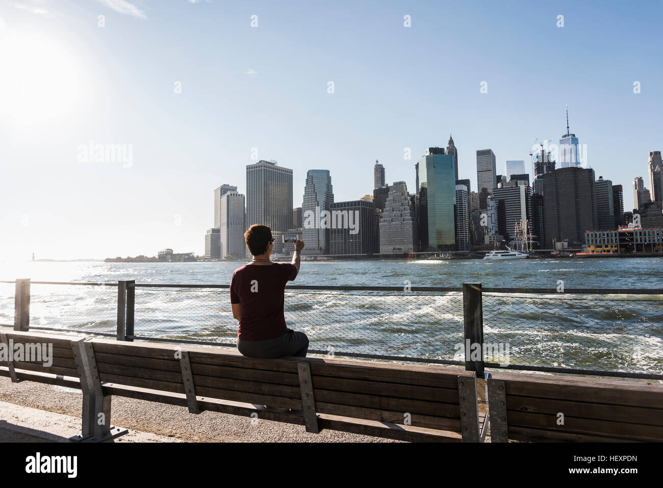 USA, Brooklyn, back view of woman taking picture of Manhattan skyline ...