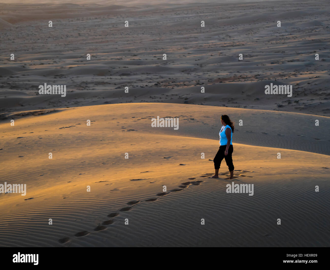 Oman, Al Raka, young woman standing on a desert dune in Rimal Al Wahiba ...