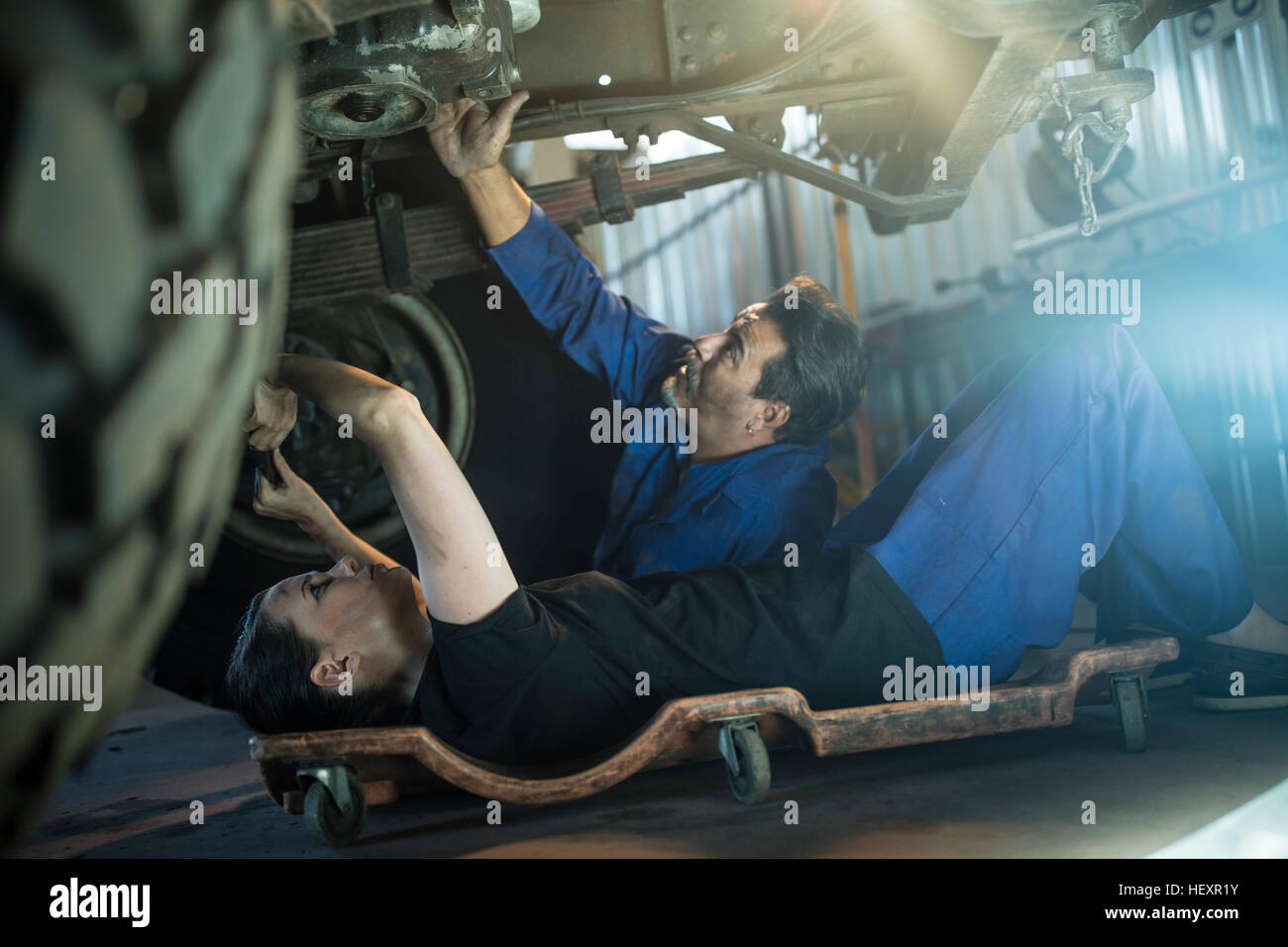 Mechanics working at fire brigade workshop, lying on creeper Stock ...