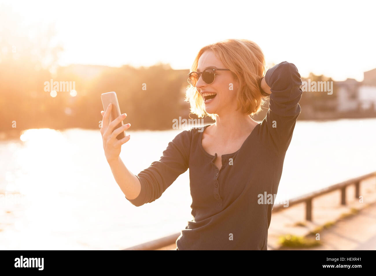 Happy young woman taking selfie with smartphone at backlight Stock ...