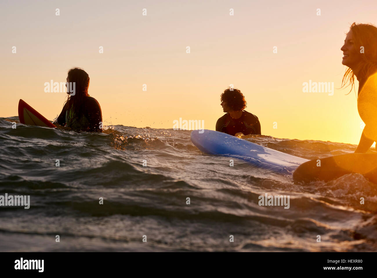 Three surfers in the sea at sunset Stock Photo - Alamy