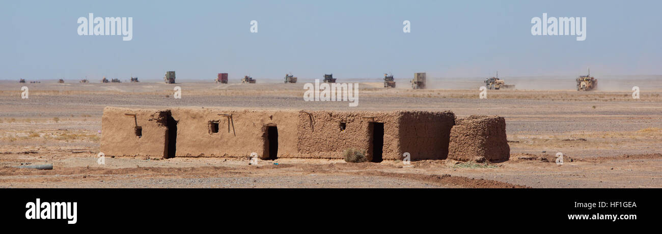 A line of vehicles drive along a desert road behind a solitary compound ...