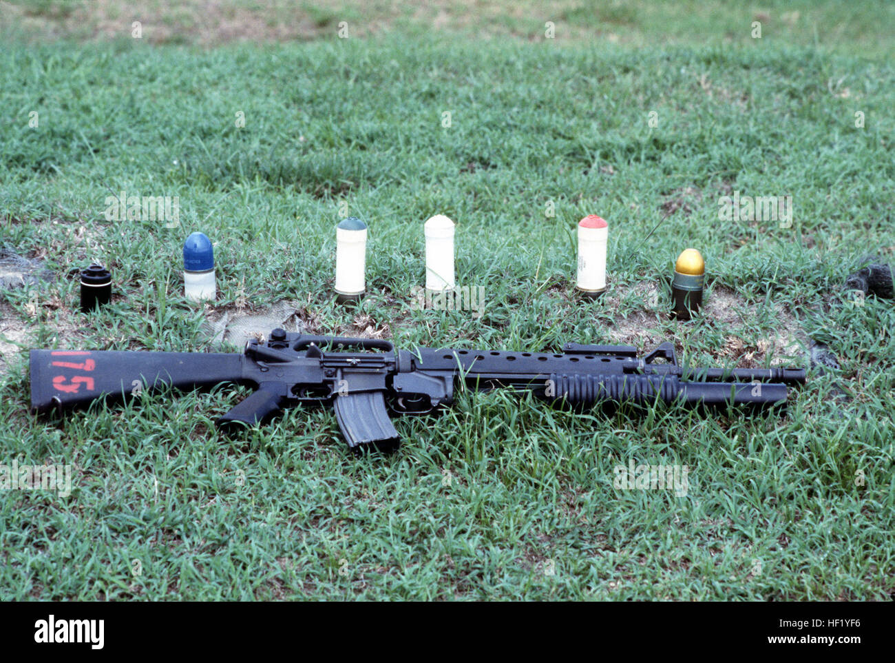 An M16A2 rifle equipped with an M203 grenade launcher lies in the grass ...