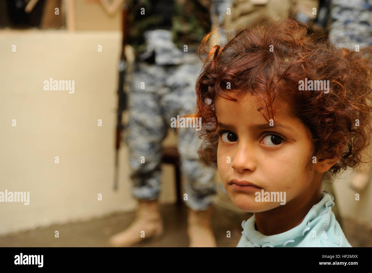 An Iraqi girl stands outside as Iraqi national policemen search her ...