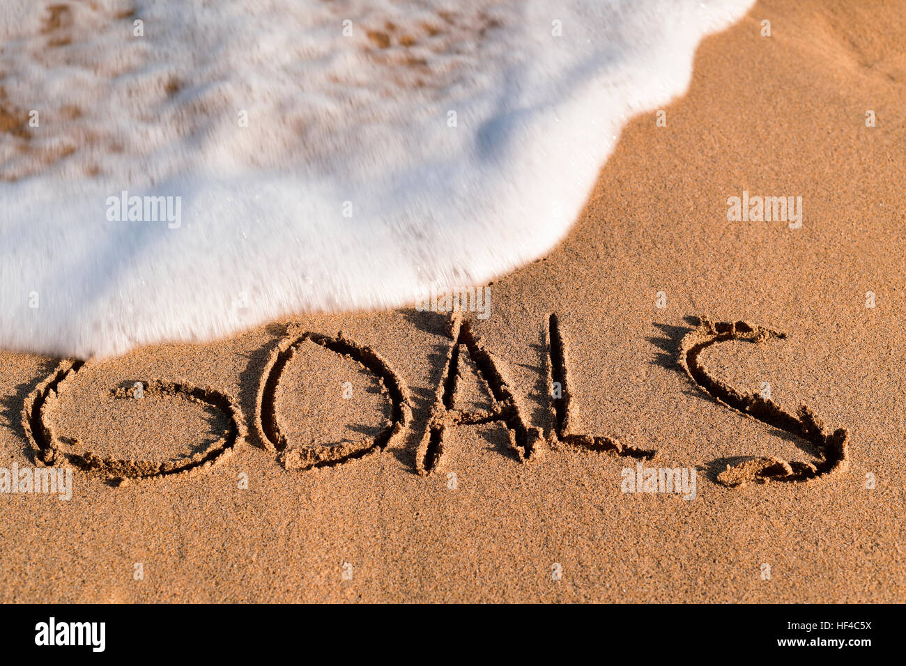 the word goals written in the sand of a beach and a wave of seawater ...