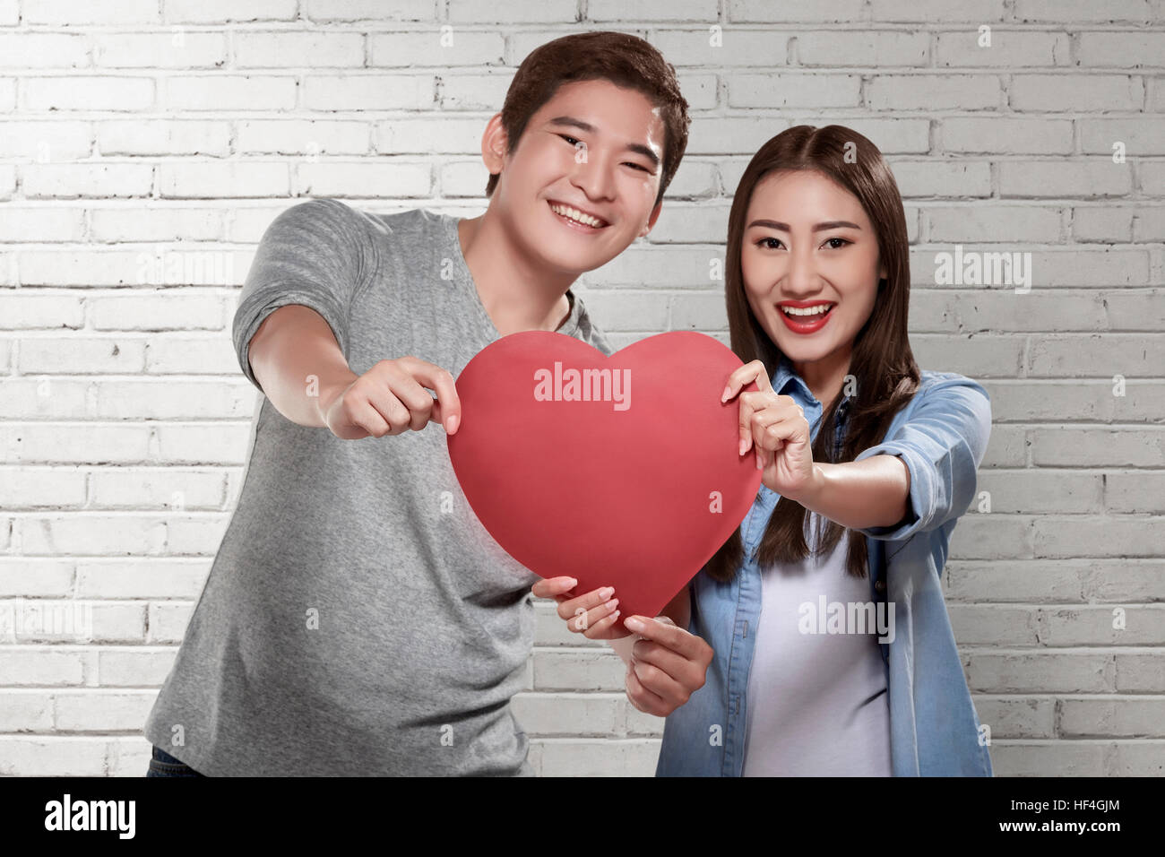 Cute asian couple standing holding red heart over white wall background ...