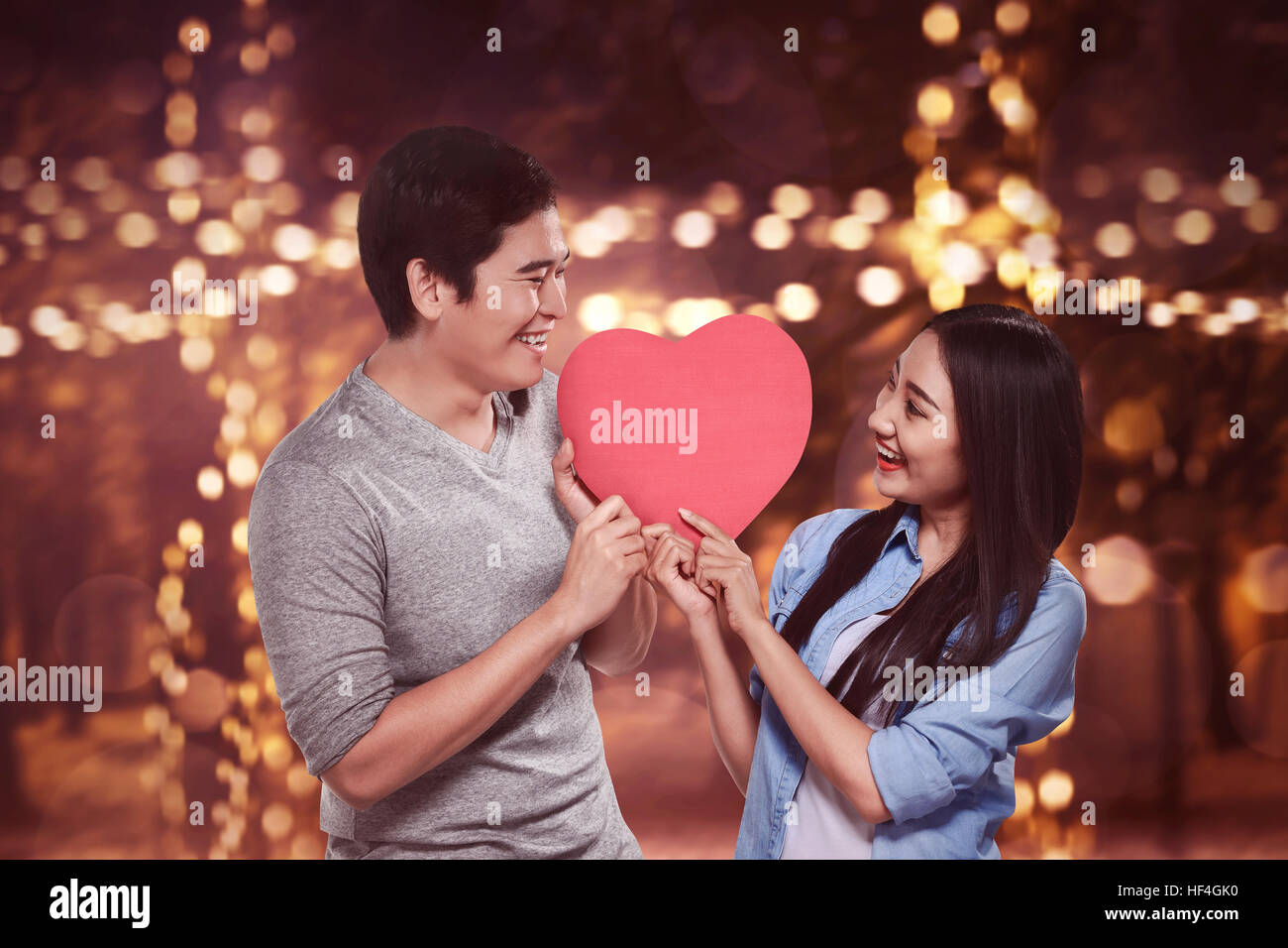 Romantic asian couple holding red heart shape while looking each other ...