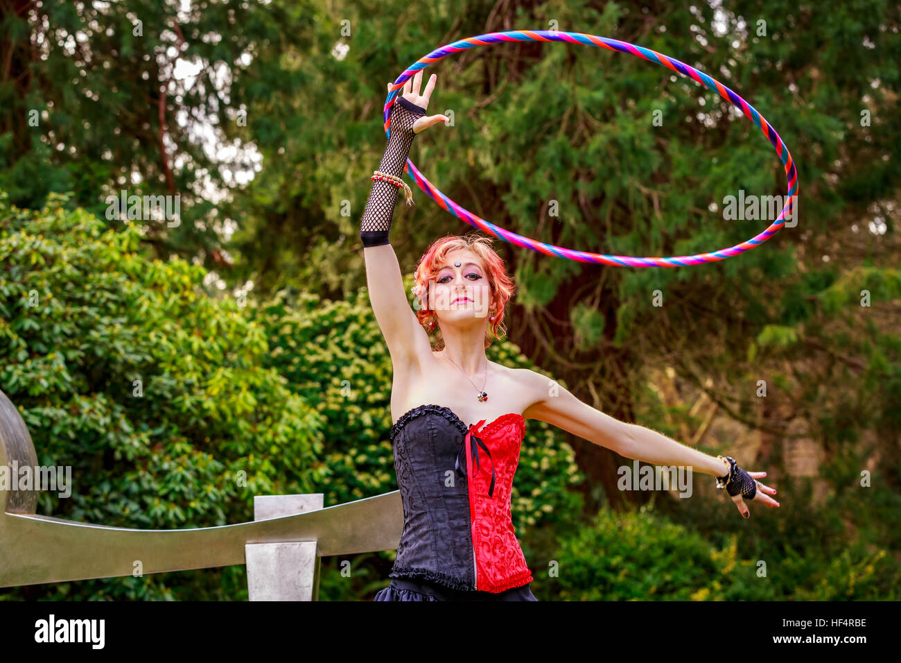 Young beautiful woman in circus costume play with hula hoop in the park ...
