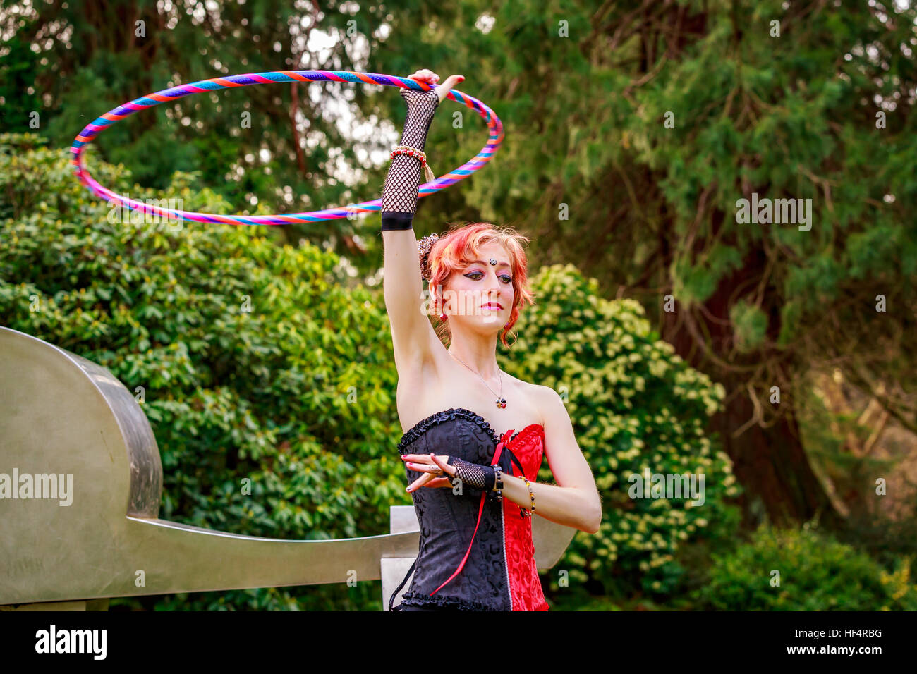 Young beautiful woman in circus costume play with hula hoop in the park ...